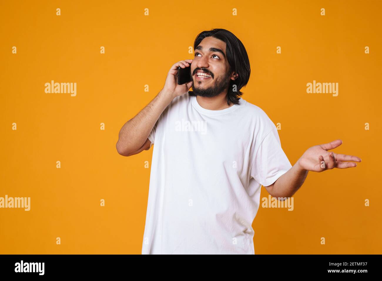 Happy young indian man using mobile phone isolated over yellow ...