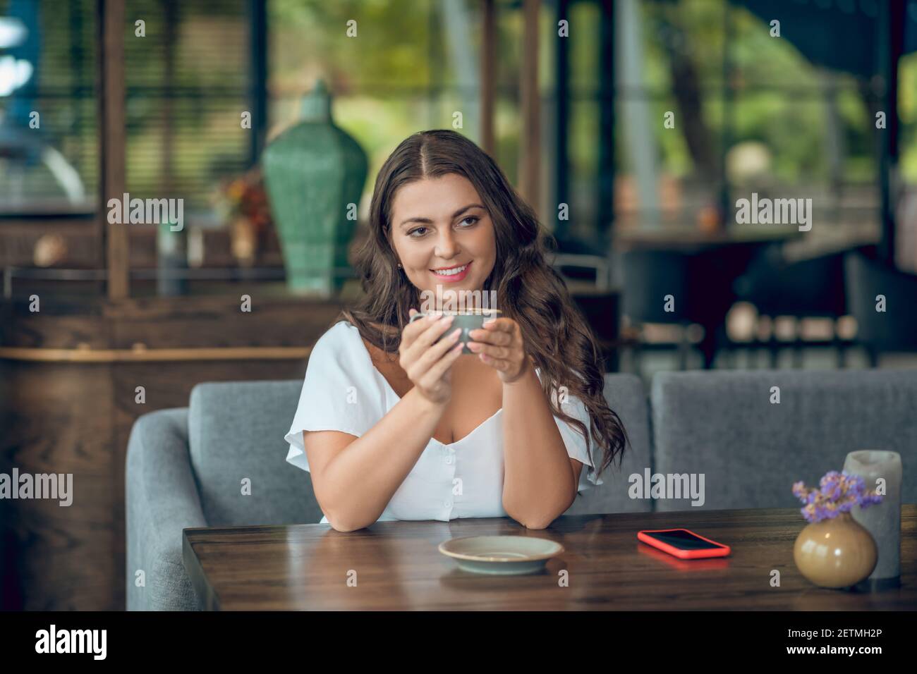 Smiling beautiful woman at table drinking coffee Stock Photo - Alamy