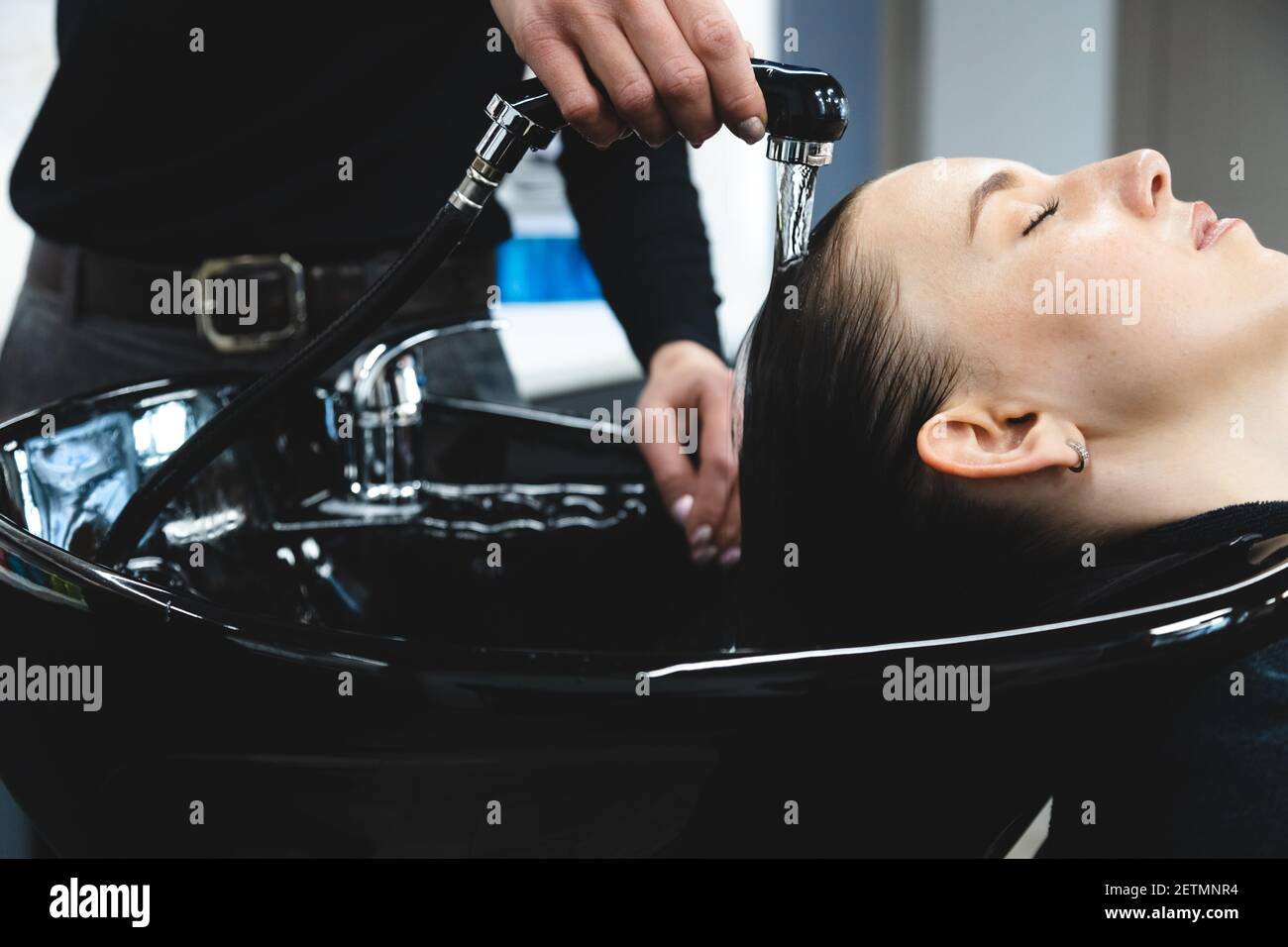 Master woman hairdresser gently washes the girl's hair with shampoo and ...