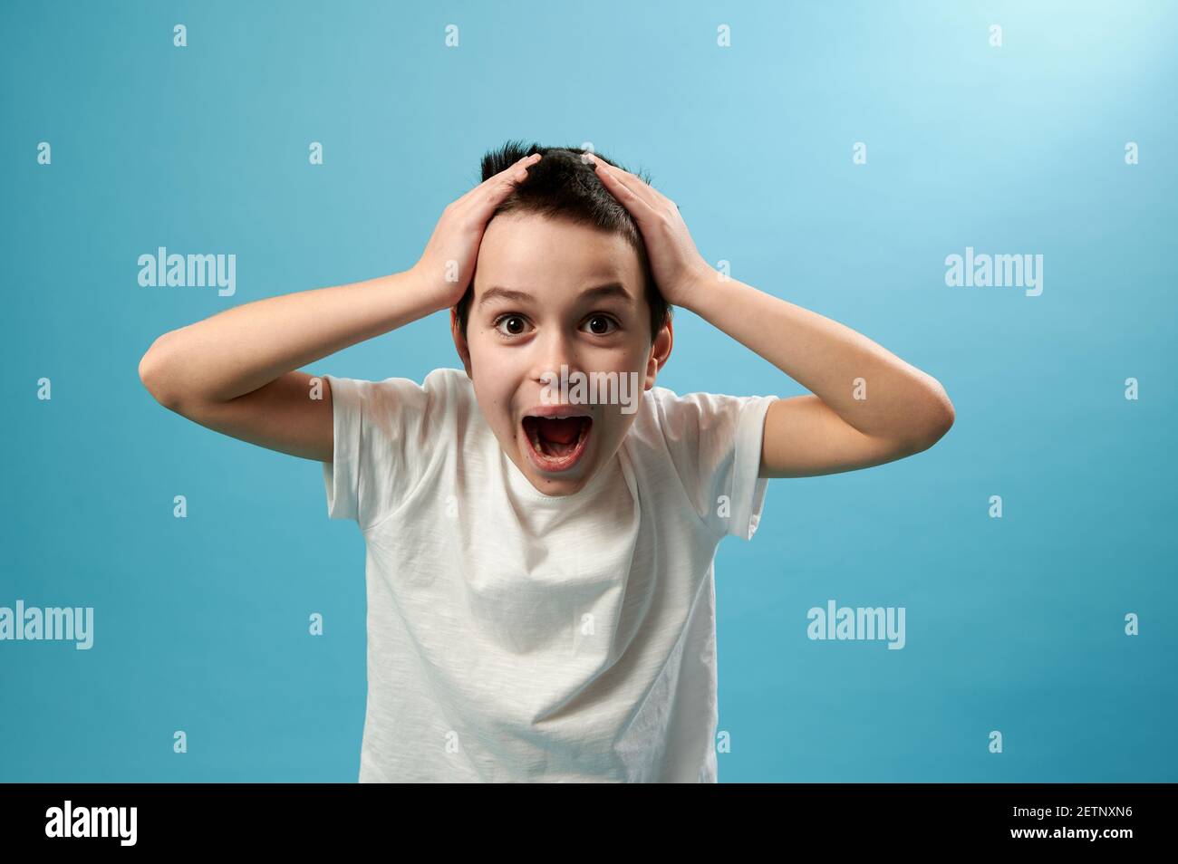 Shocked boy screams and laughs with his hands on his temples ...