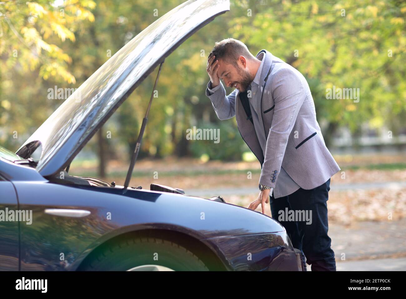 Man looking under the hood of the car trying to figure out what went ...