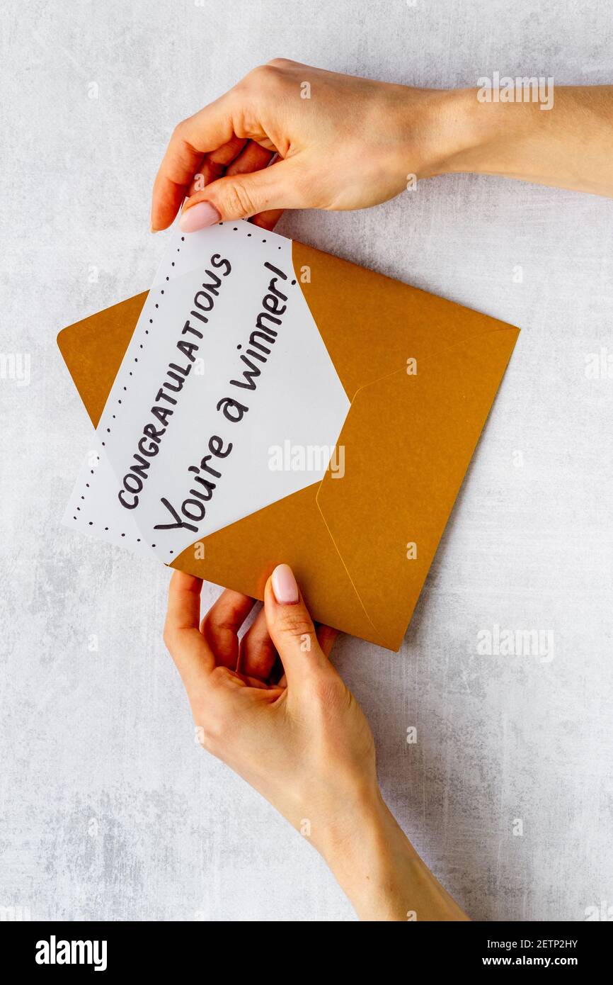 Hands holding award congratulation card in golden envelope. Text You're ...
