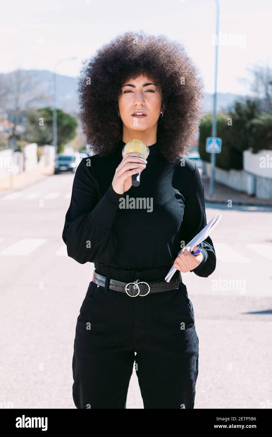 Female television reporter journalist with afro hair reporting on a ...