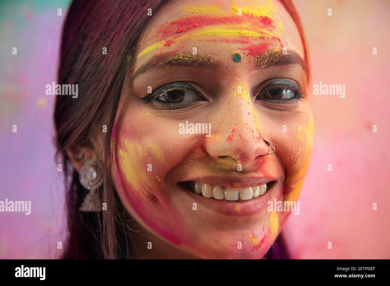 A YOUNG WOMAN WITH GULAL ON HER FACE LOOKING AT CAMERA AND SMILING ...
