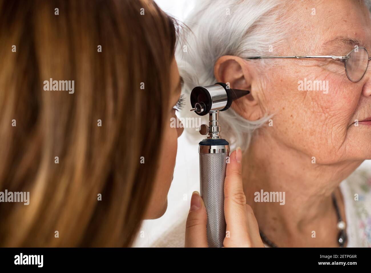 Doctor holding otoscope and examining ear of senior woman in ambulance ...