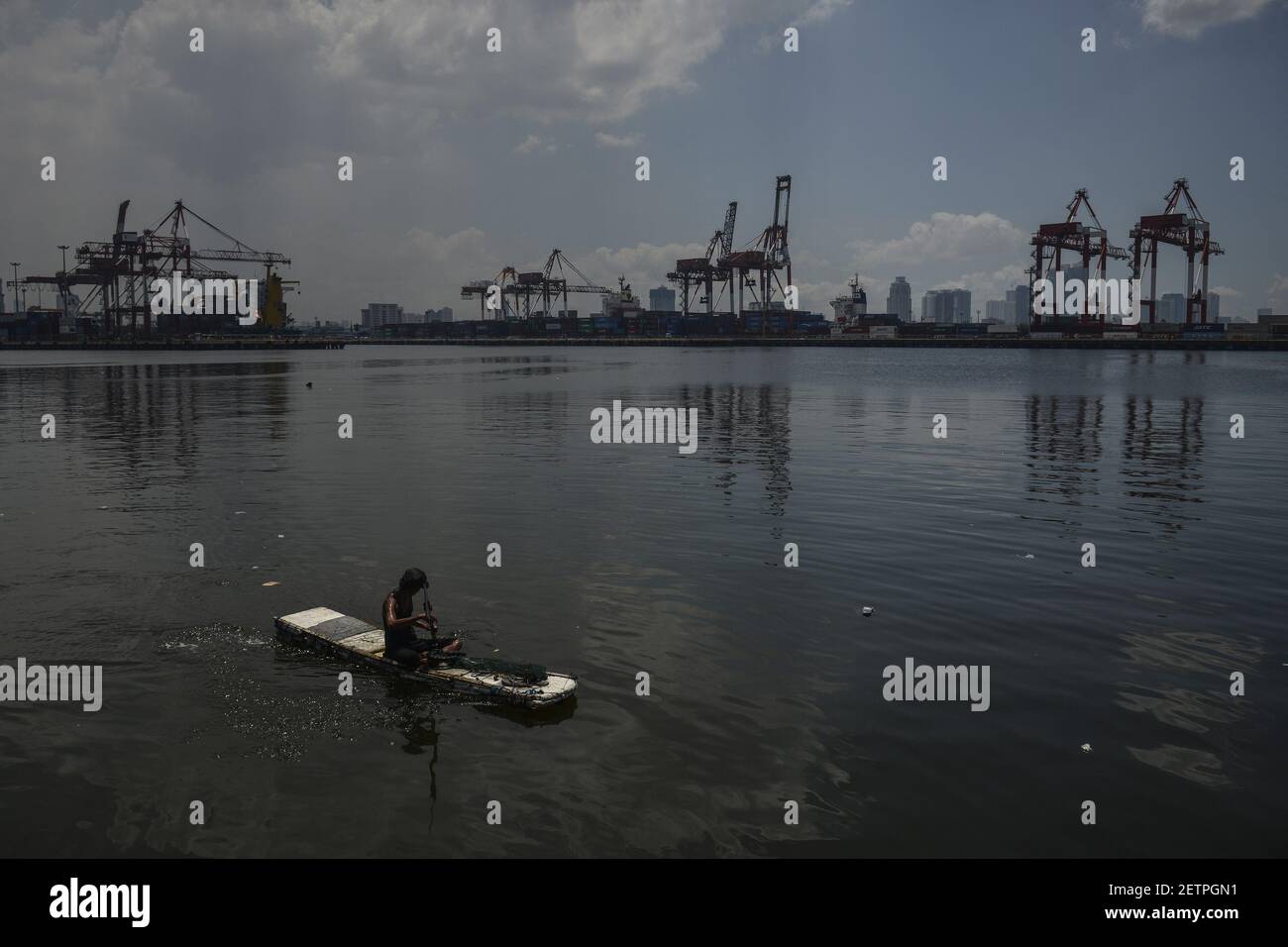 A resident paddles his makeshift boat to collect recyclables along a ...