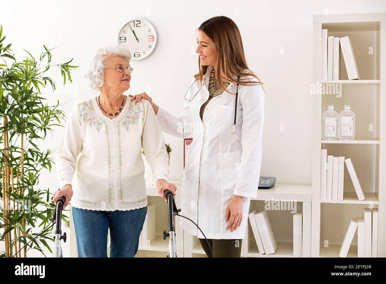 Beautiful young doctor helping senior woman walking with a walker in ...
