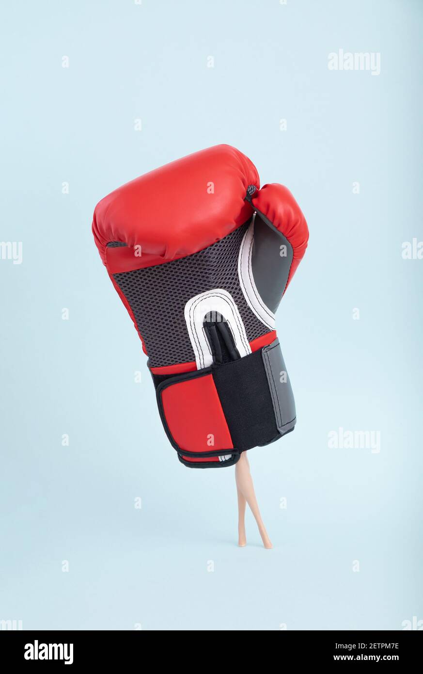 Plastic doll legs in heavy staggering boxing glove on minimal blue ...