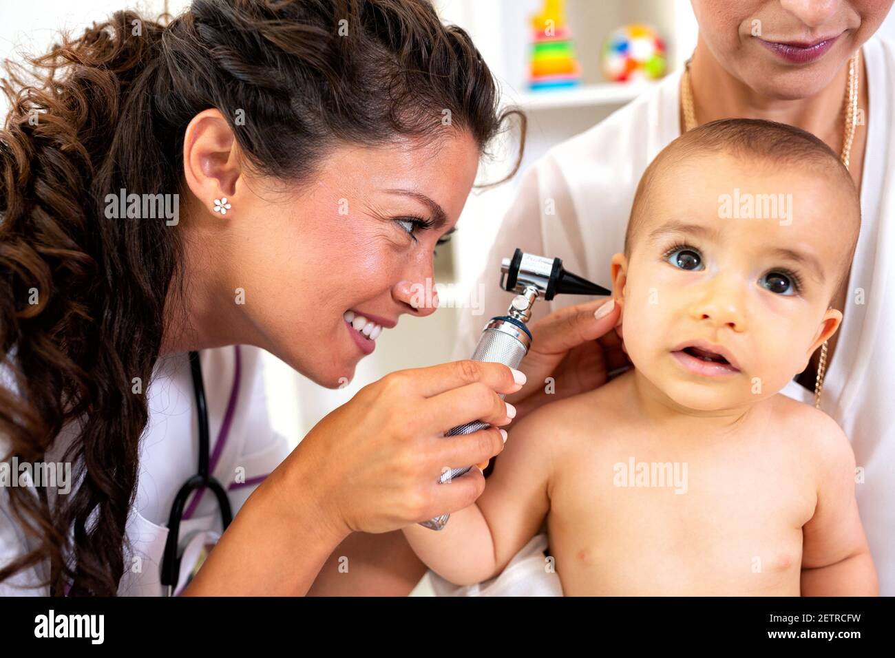 Attractive doctor examining the ear of young baby providing ...