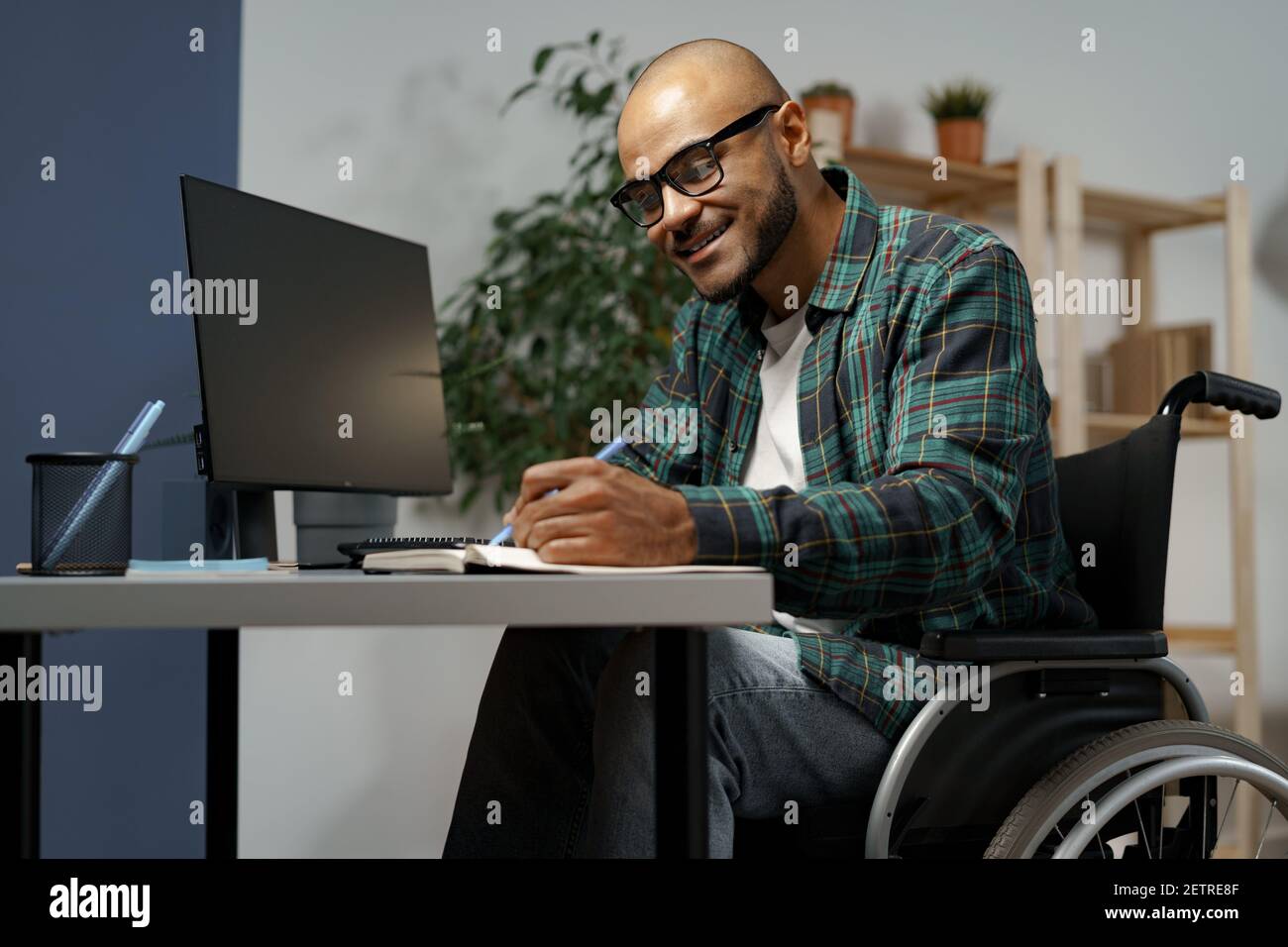 Disabled young african american man in wheelchair using computer while ...