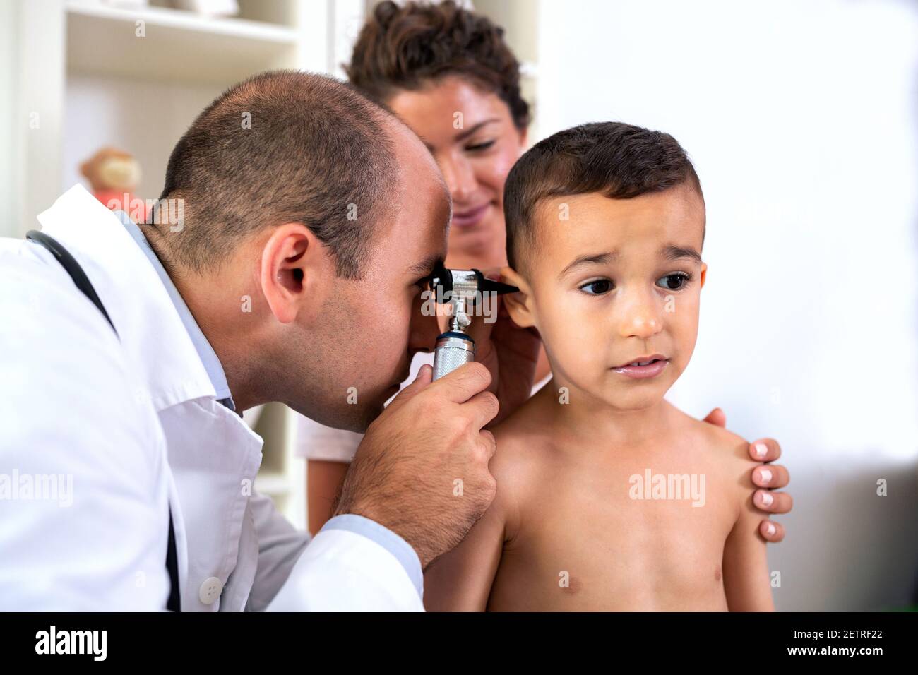 Child specialist looking inside of an ear of a young patient held by ...