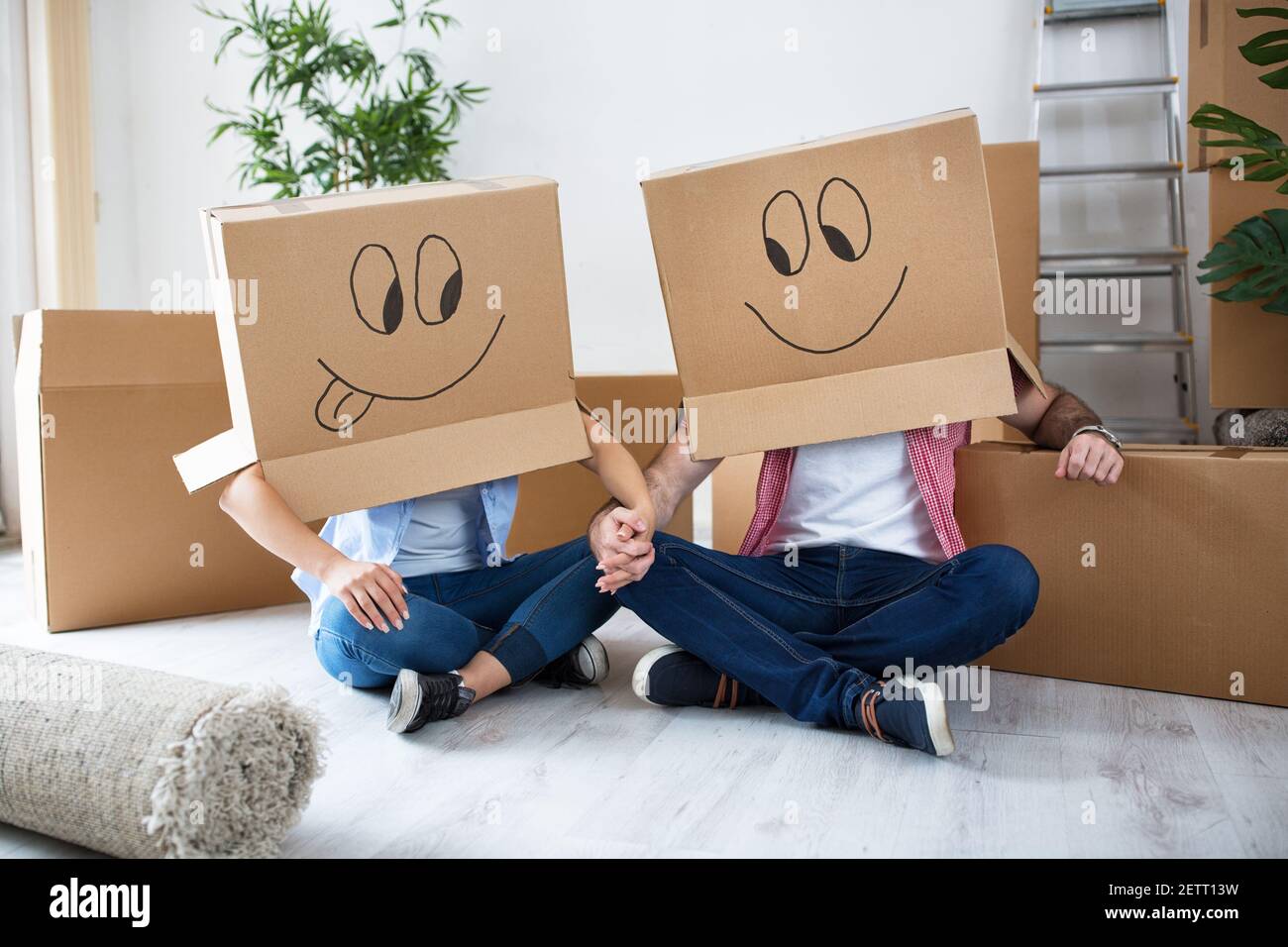 Funny happy couple sitting on floor wearing smiley cardboard boxes ...