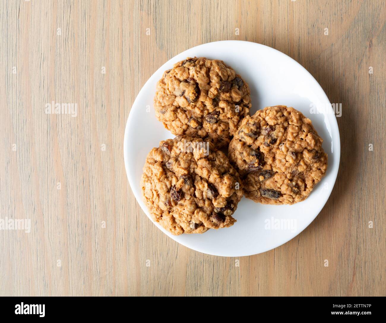 Overhead view of two homemade oatmeal raisin cookies on a white plate ...