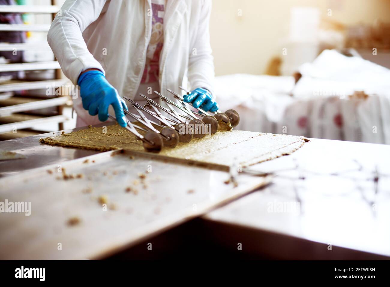 Close up view of the worker cutting baked cookie dough on a tin plate ...