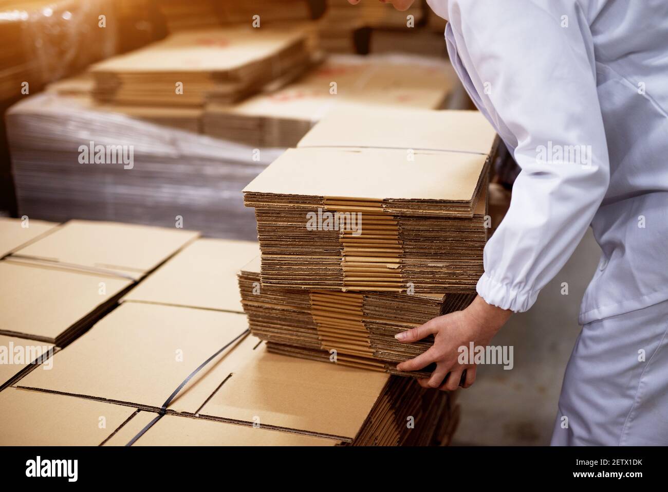 Close up of young female worker picking up stacks of folded cardboard ...
