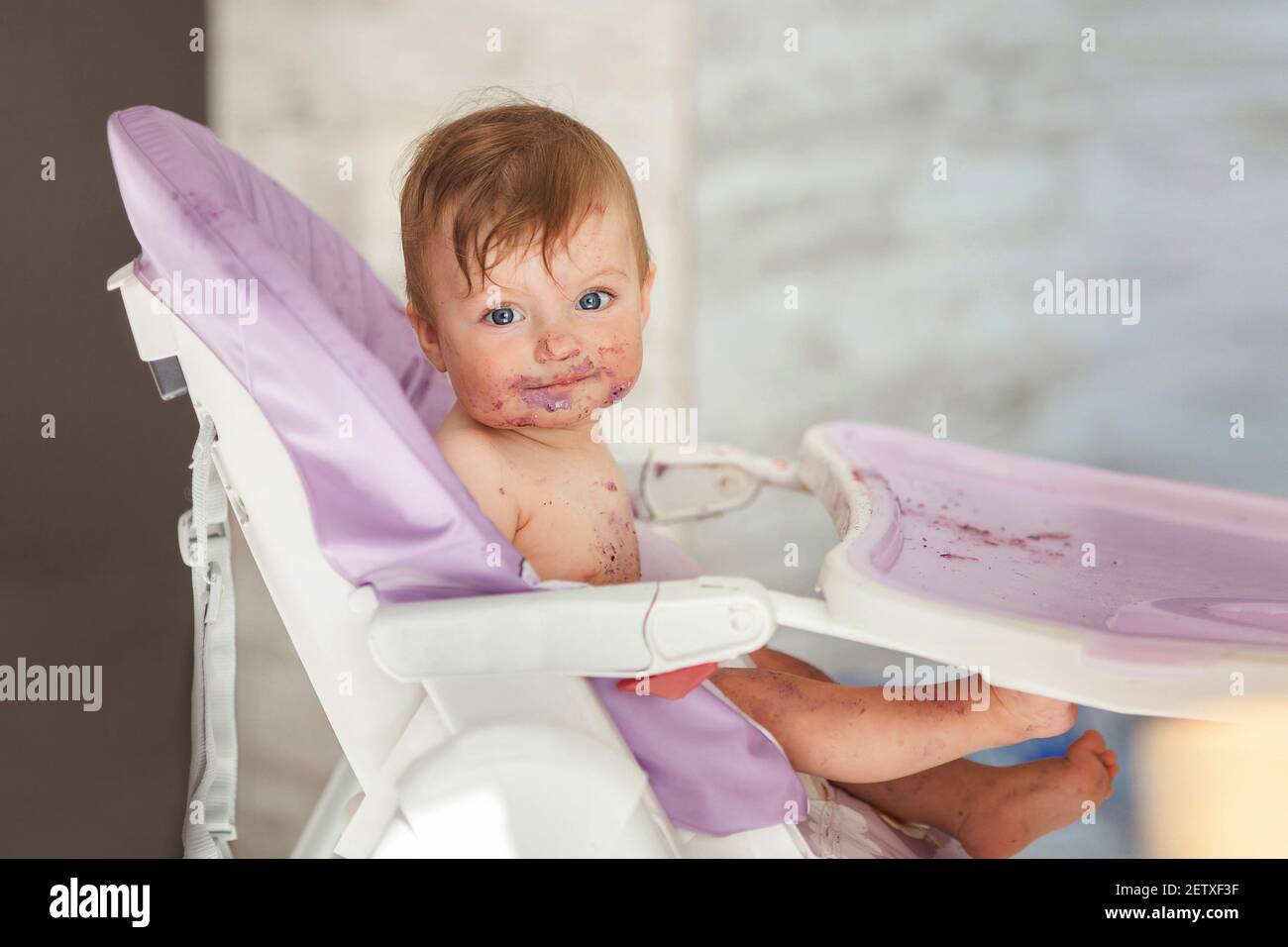 Adorable baby eating on baby chair and making a mess. Little baby girl ...