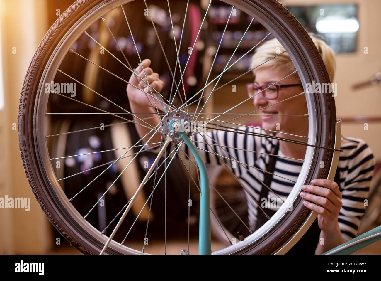 Beautiful cheerful woman tightening bicycle wheel screws in the garage ...