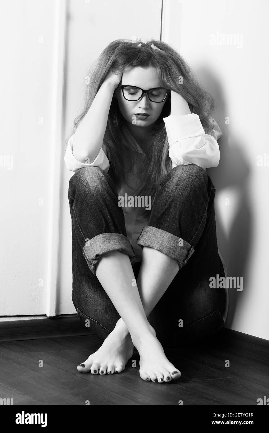 sad young woman in eyeglasses sitting on floor looks down, monochrome ...