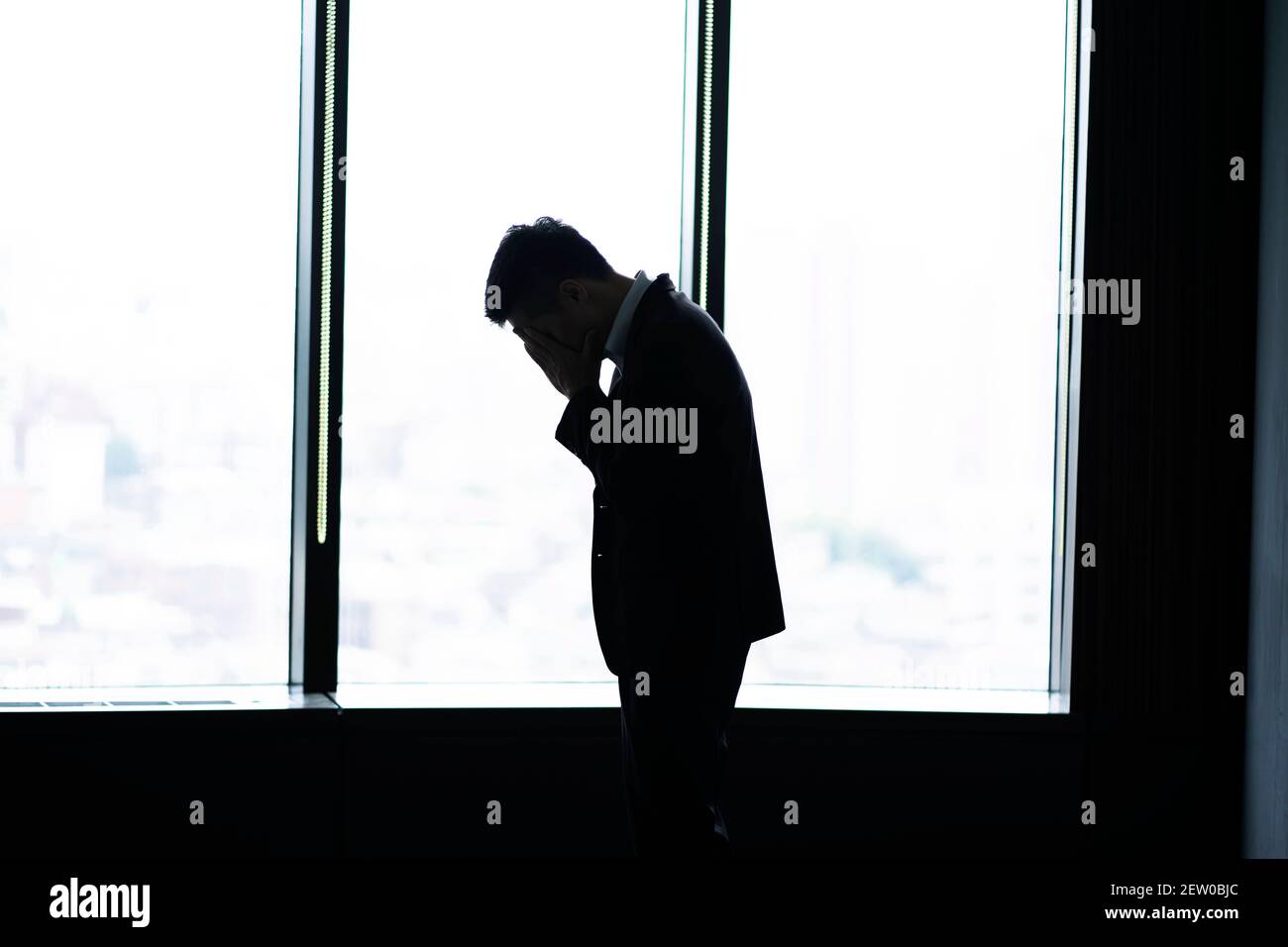 Frustrated businessman standing by window Stock Photo - Alamy