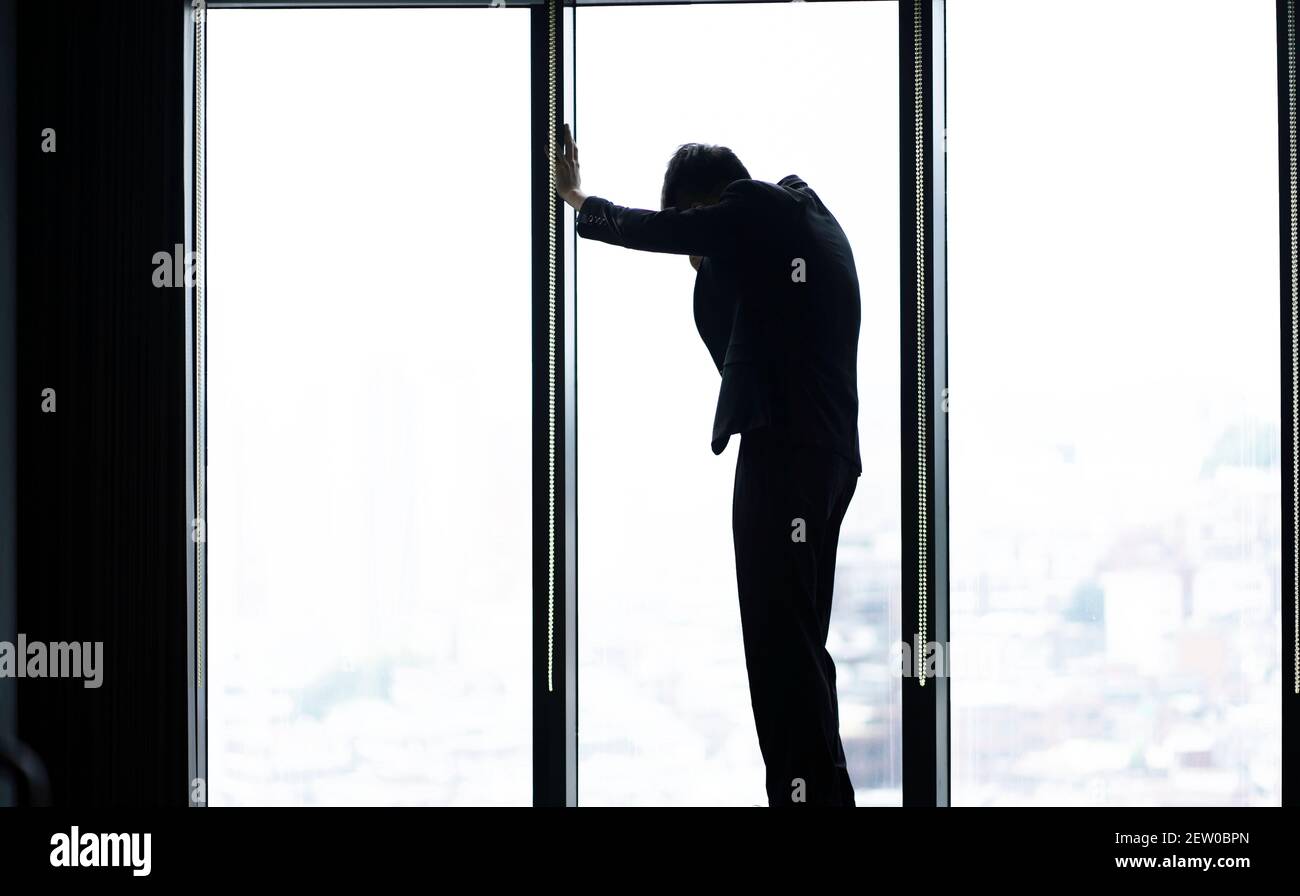 Pensive businessman leaning against window Stock Photo - Alamy
