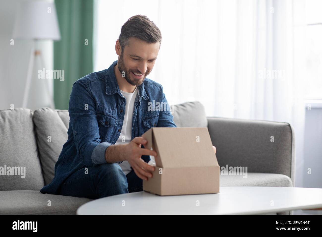 Happy man unpacking delivery box, home interior Stock Photo - Alamy