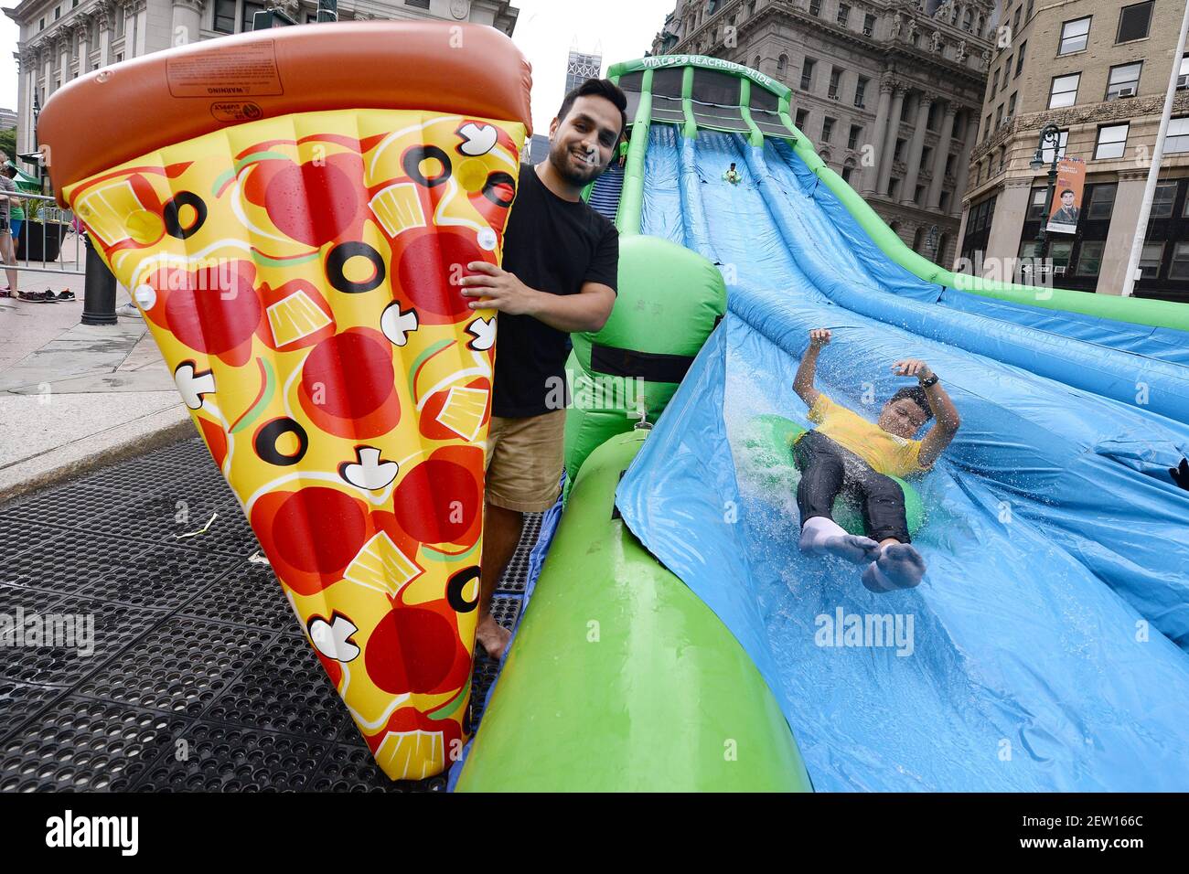 A man poses with a pizza shaped inflatable raft as a man slides down a ...