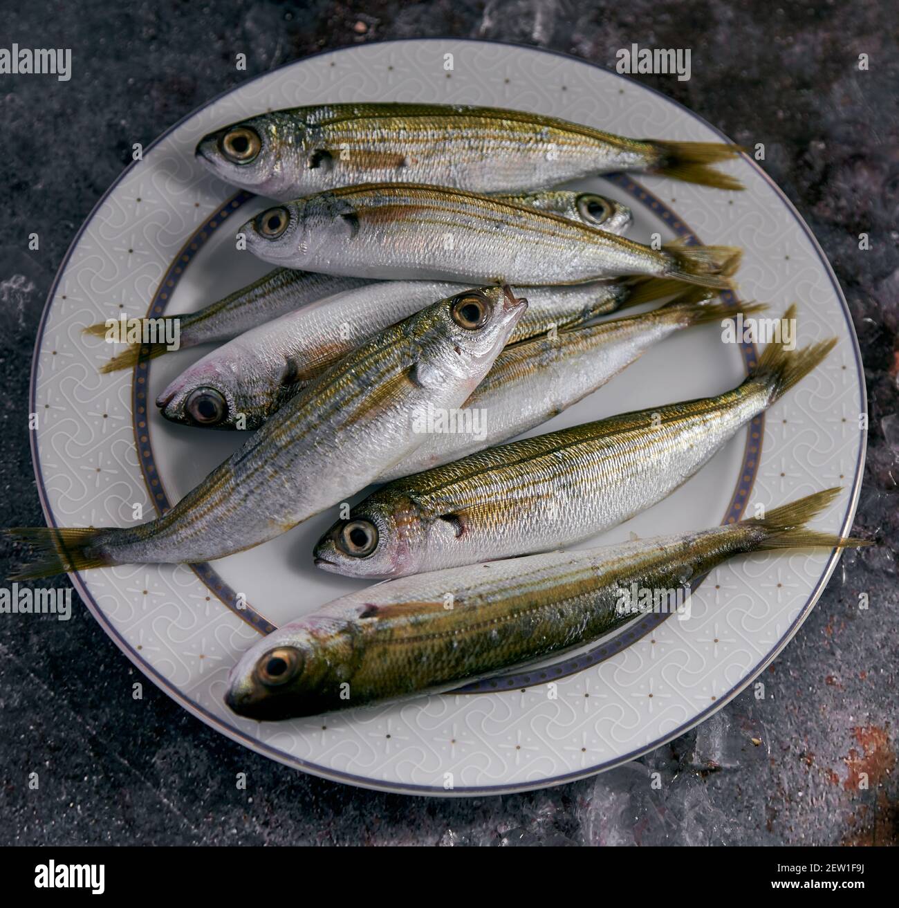 From above of uncooked fish with tails and eyes on round shaped plate ...