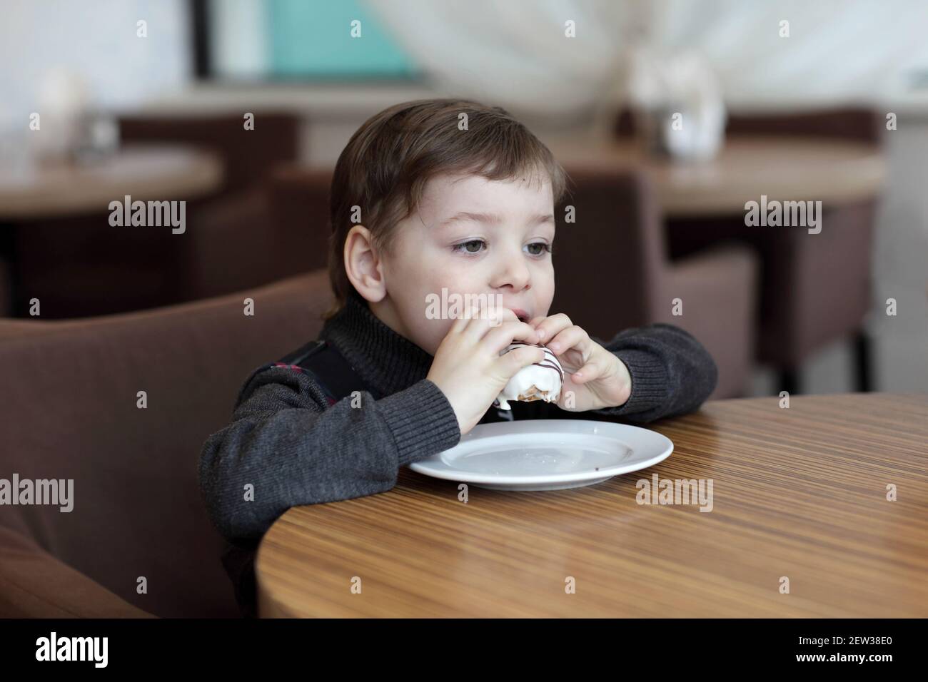 Child biting eclair at table in the cafe Stock Photo - Alamy