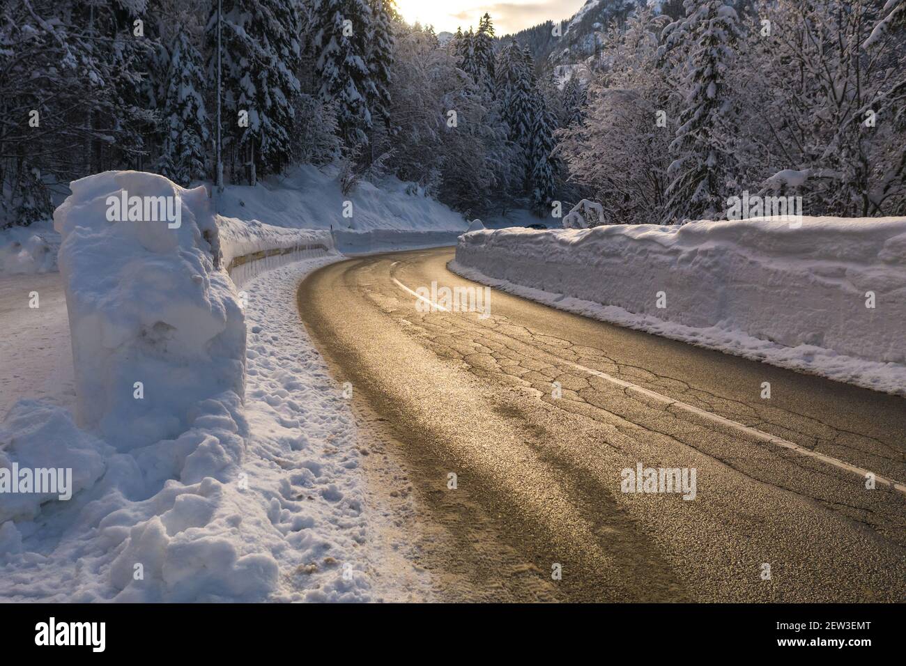 Driving on a snowy winter road through a forest in nature with sun ...