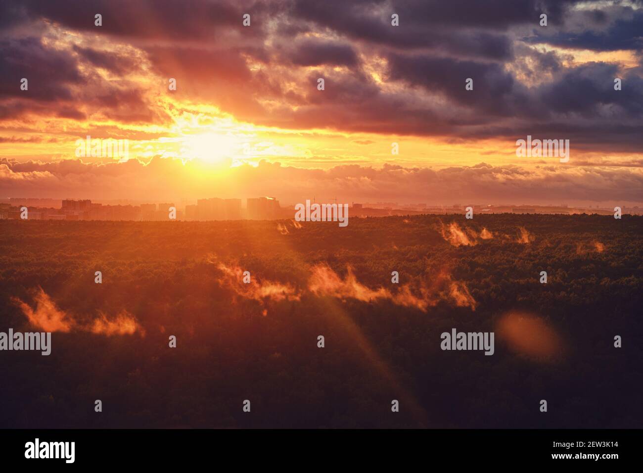 Beautiful setting red sun behind city houses, fog and sun rays over ...