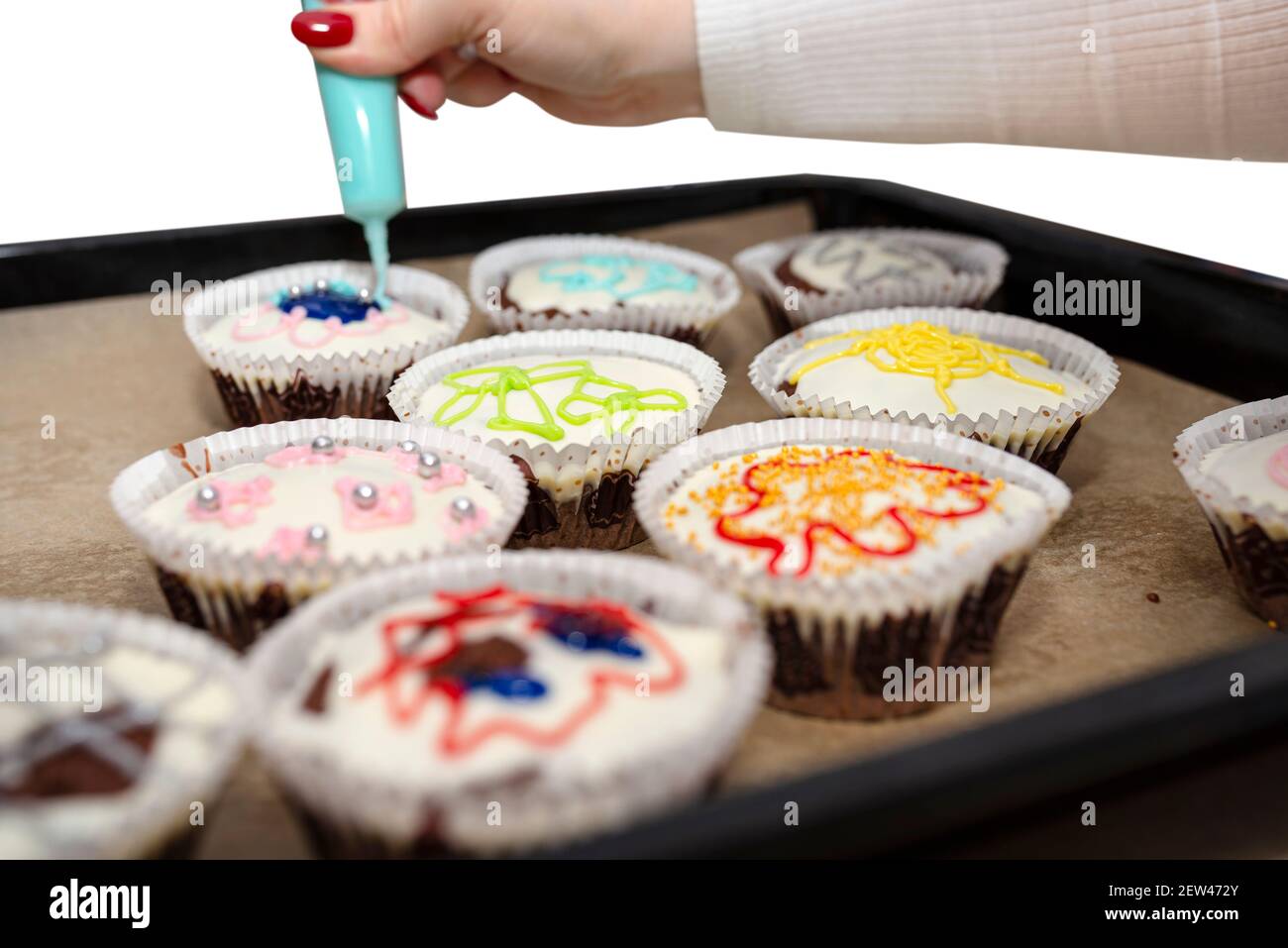 A woman squeezes colored frosting from a tube onto chocolate brown ...
