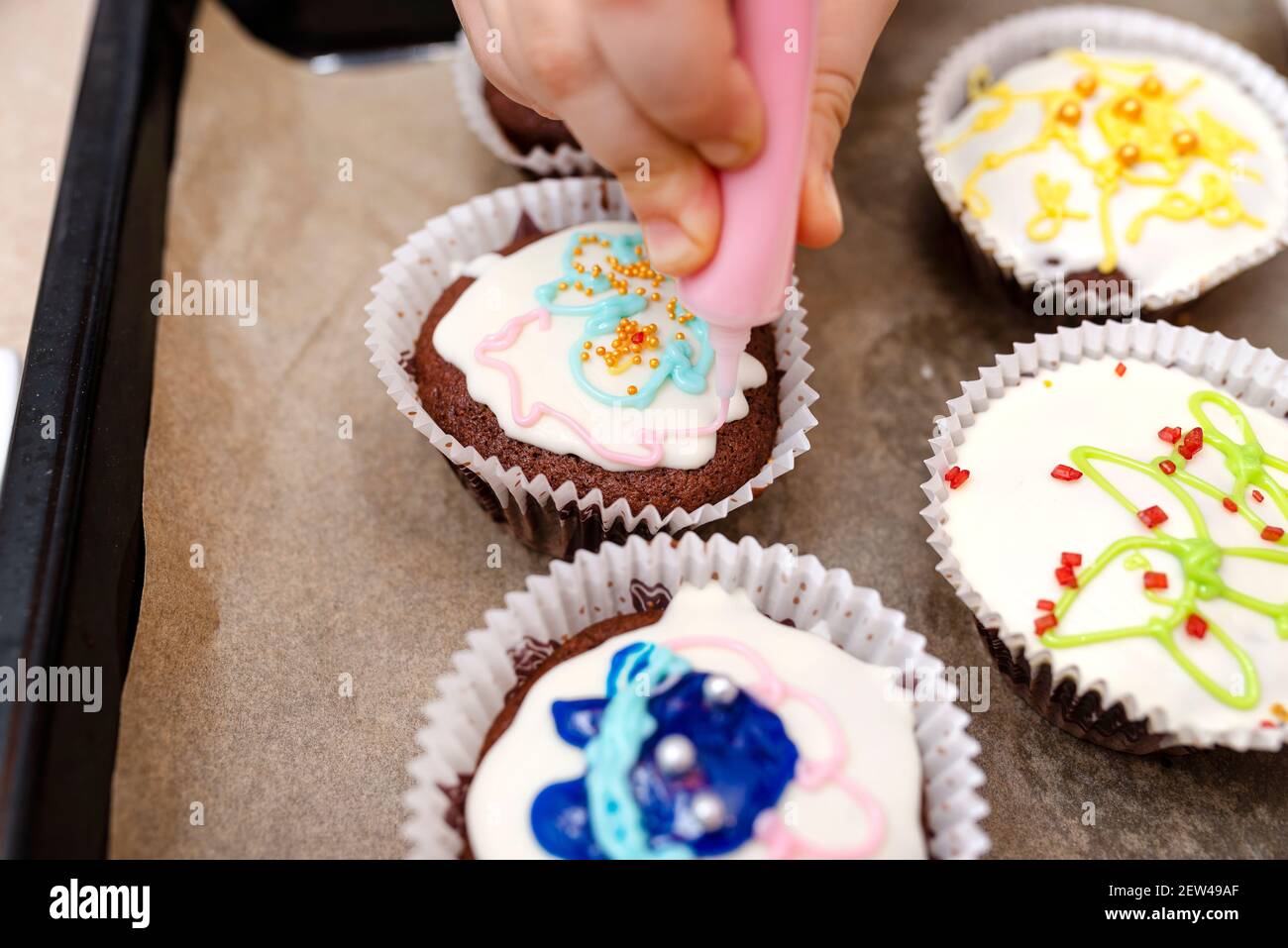 A child squeezes colored frosting from a tube onto chocolate brown ...