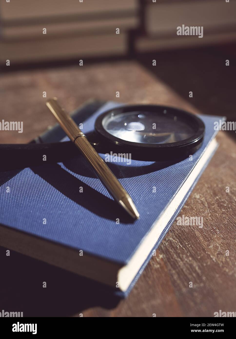 Old blue book with a magnifying glass and pen on top, on a wooden desk ...