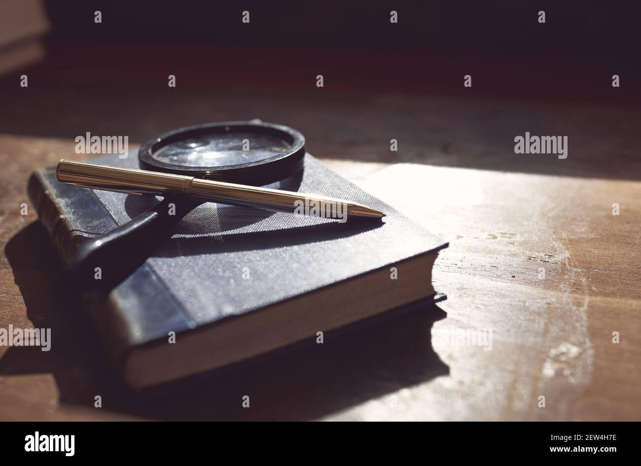Old blue book with a magnifying glass and pen on top, on a wooden desk ...