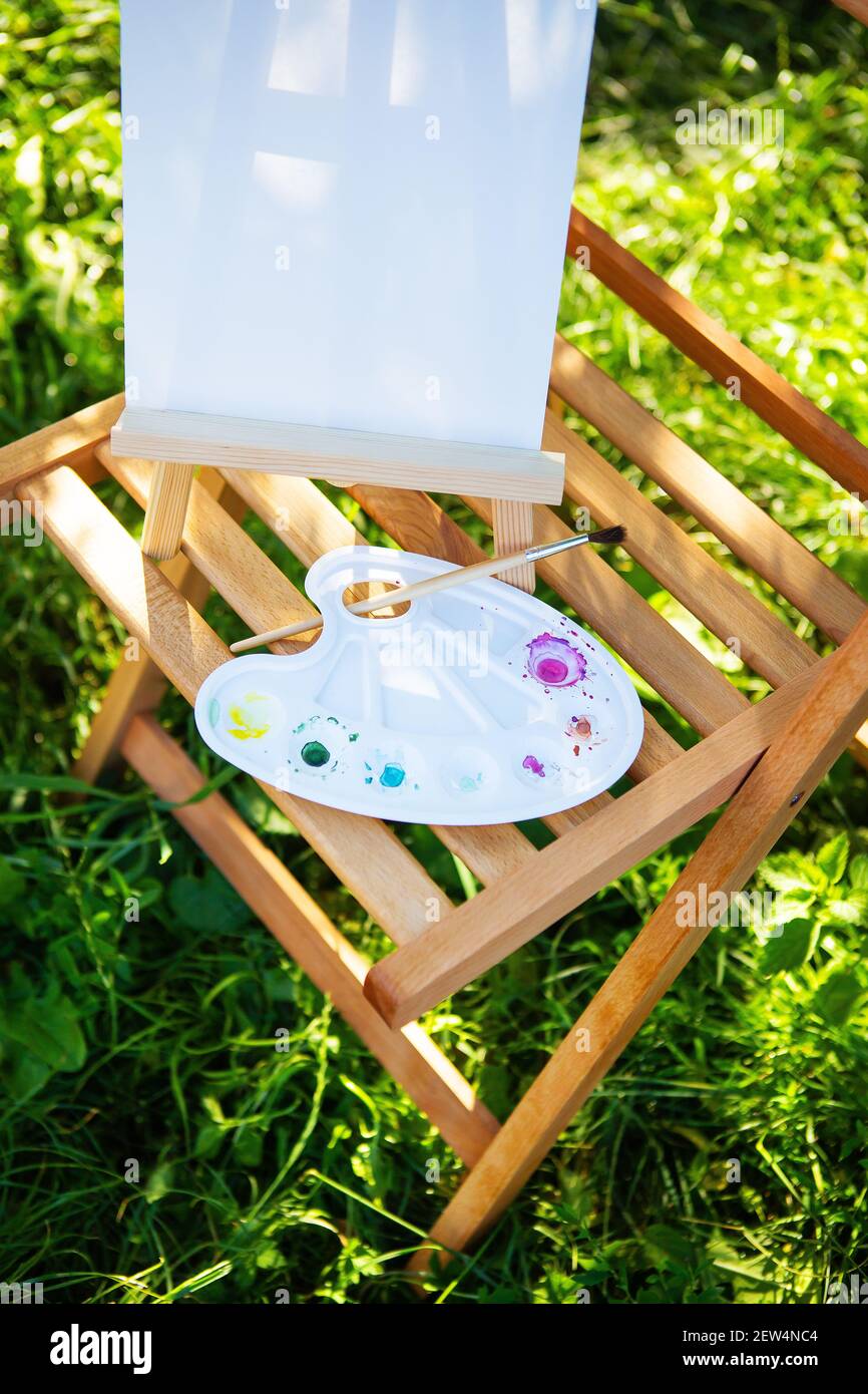A palette of watercolor multicolored paints stands on a wooden chair ...