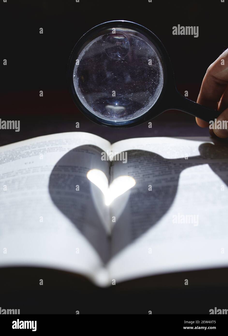 Hand holding a magnifying glass shading a heart on an open book Stock ...