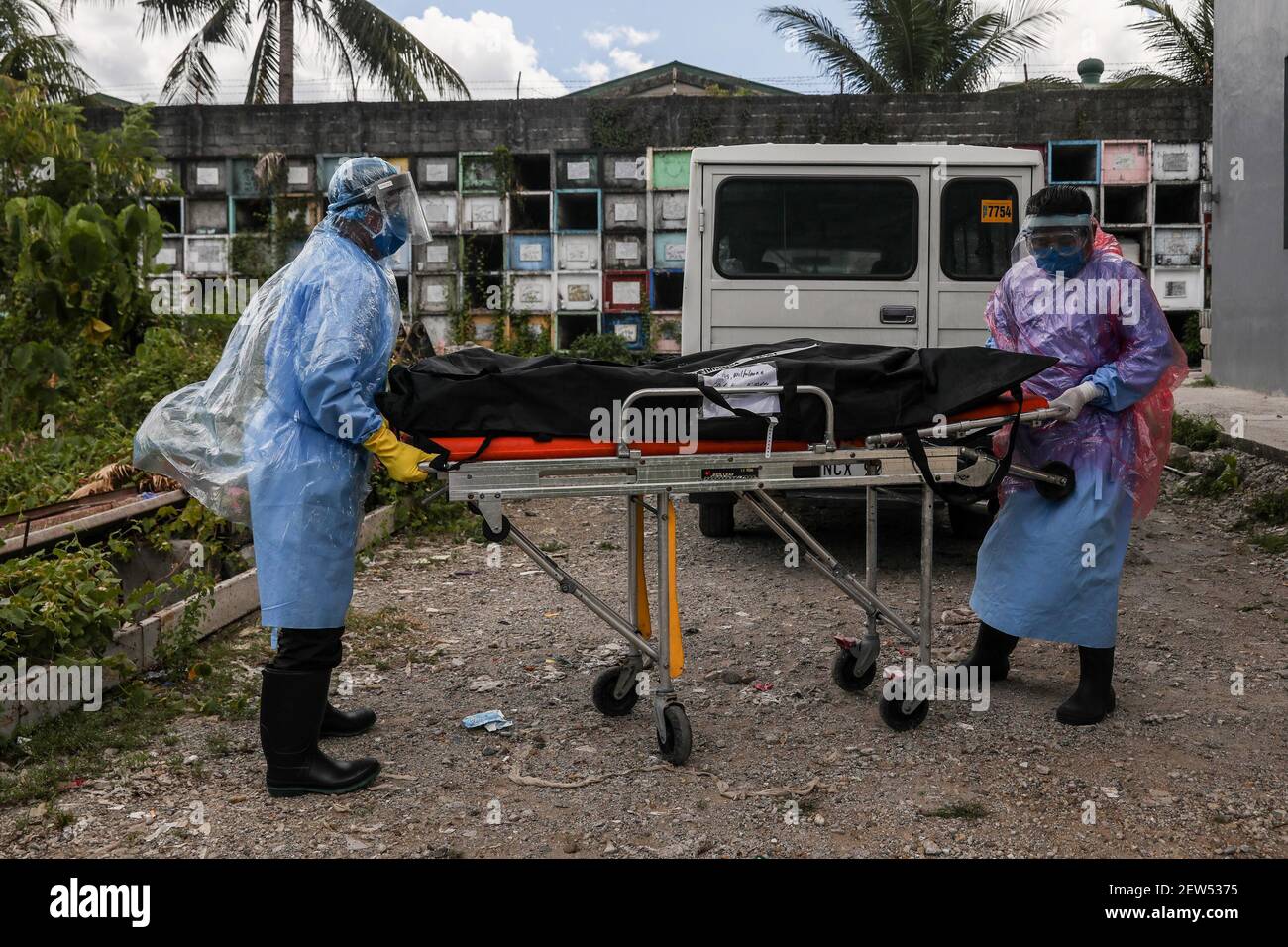 Funeral parlor workers use a stretcher as they bring a body bag inside ...