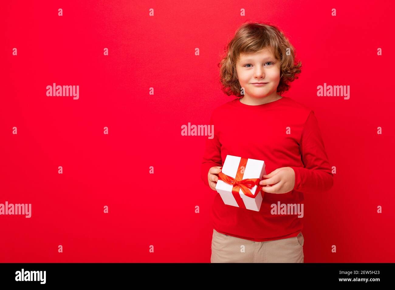 Shot of happy positive blond curly boy standing isolated over red ...