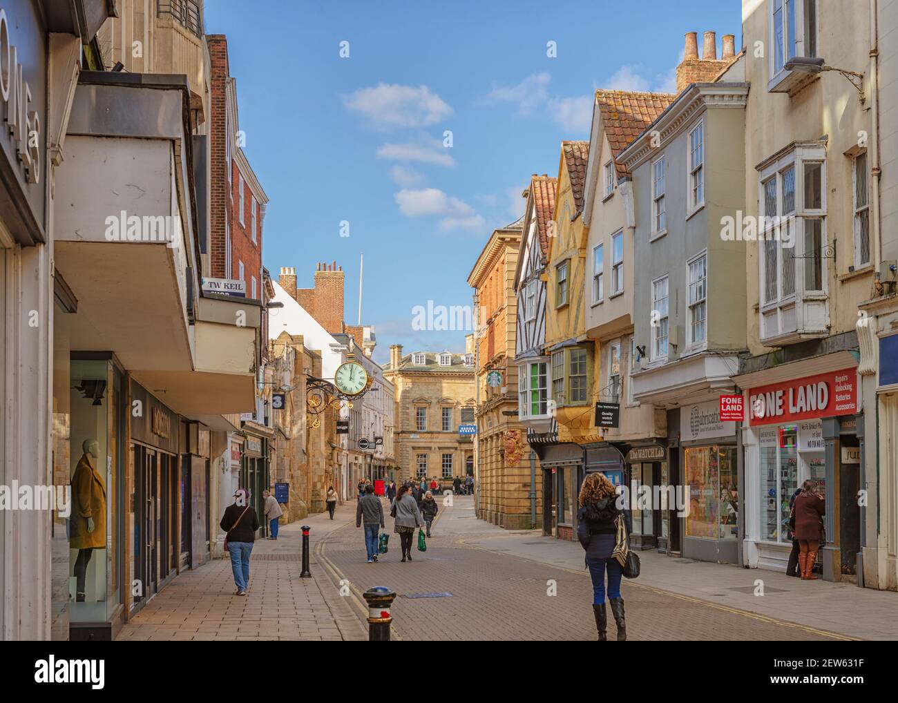Pedestrianised shopping street. Shoppers walk between the shops and a ...