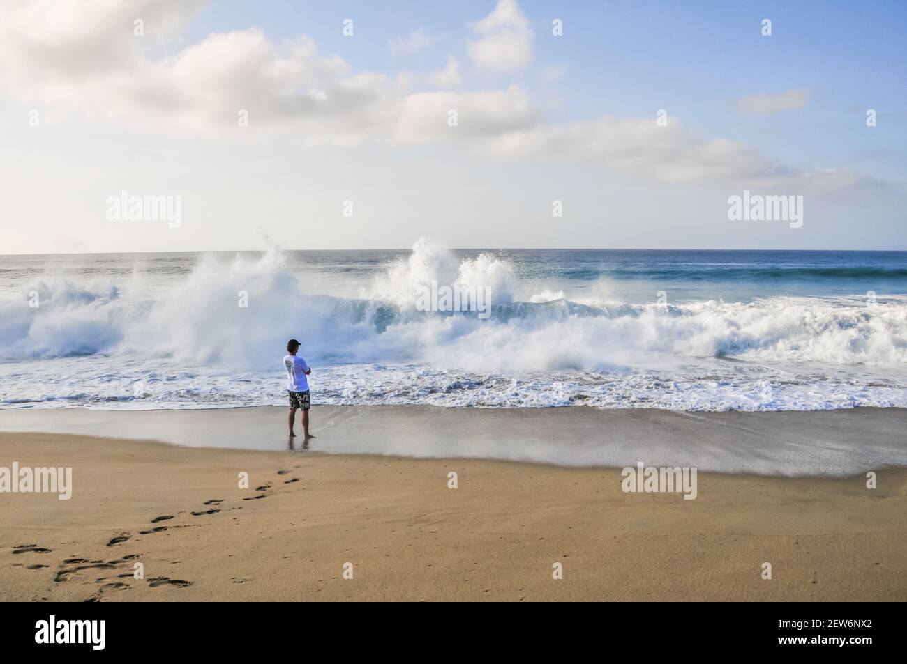 Man standing on beach watching large waves in the ocean. Footprints ...