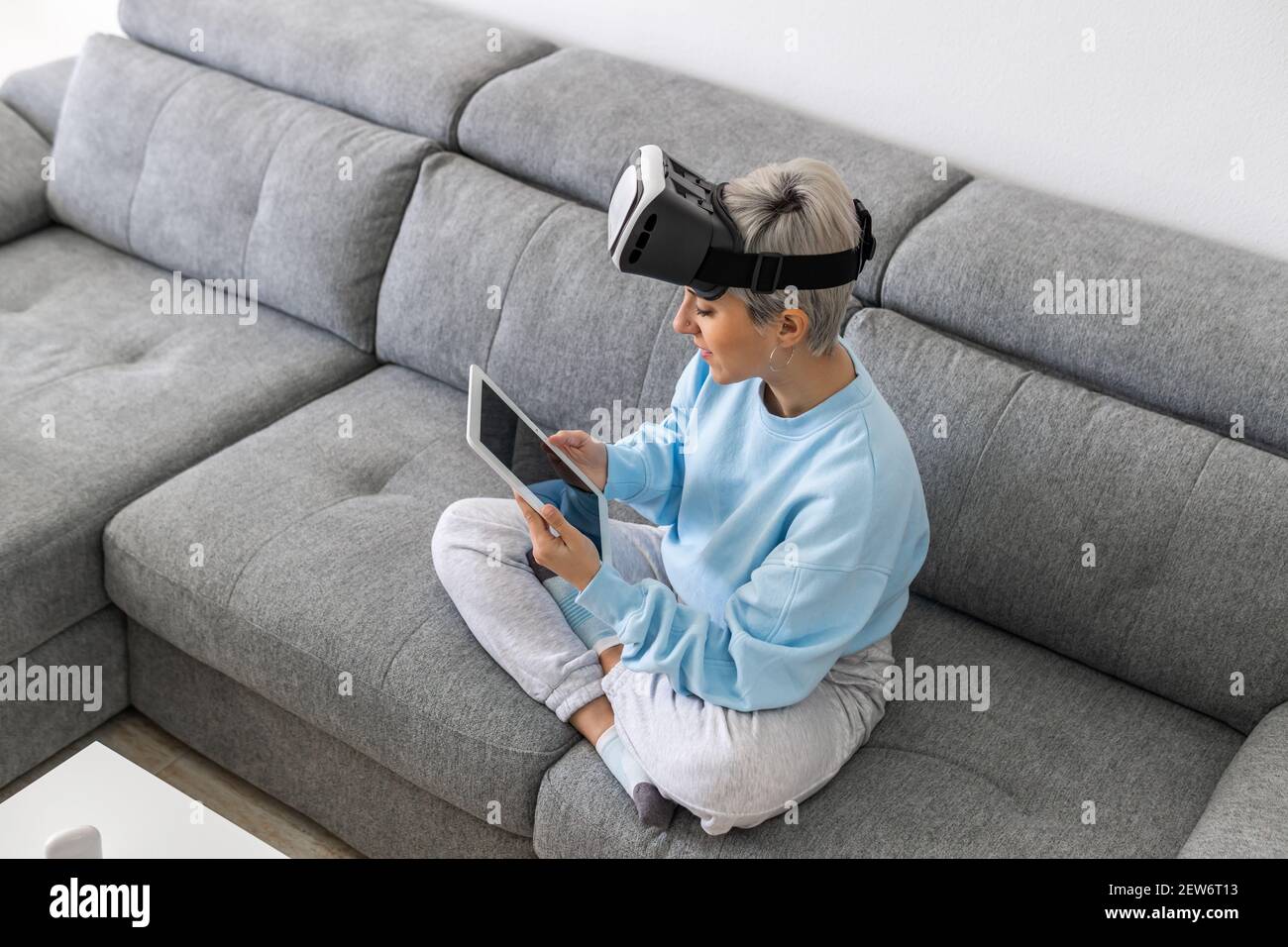An adult woman using a VR headset and a tablet while sitting on a sofa ...