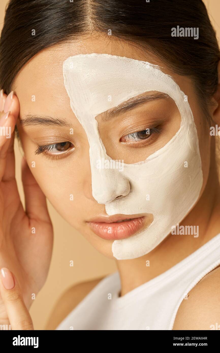 Close up shot of young woman with facial mask applied on half of her ...