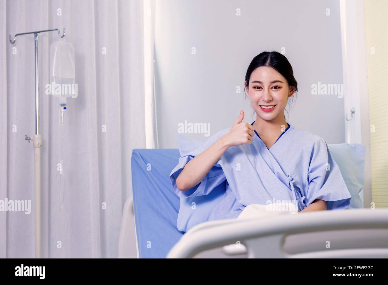 Portrait of a smiling Asian young female patient sitting on hospital ...