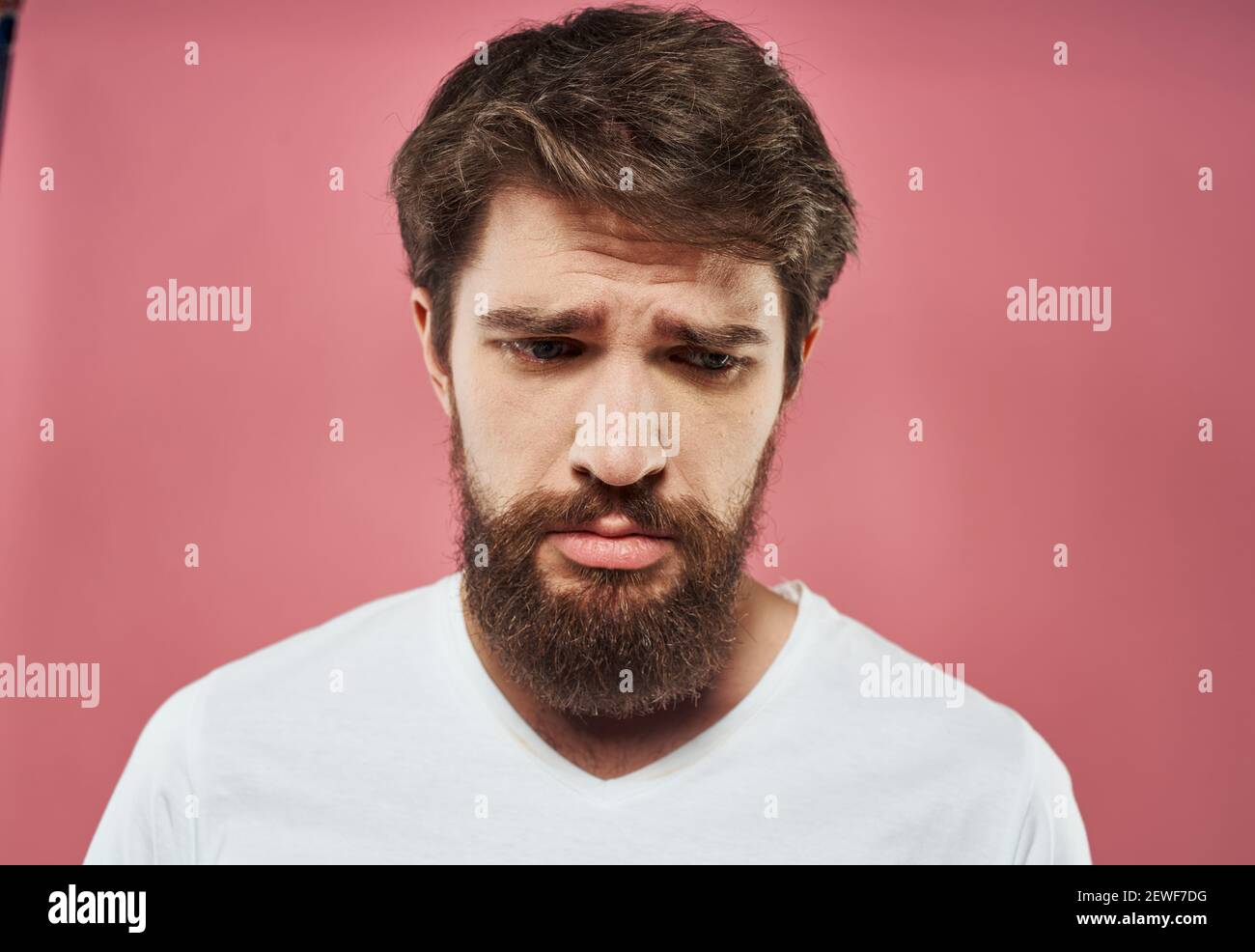 Sad man crying on a pink background in a white t-shirt cropped view ...