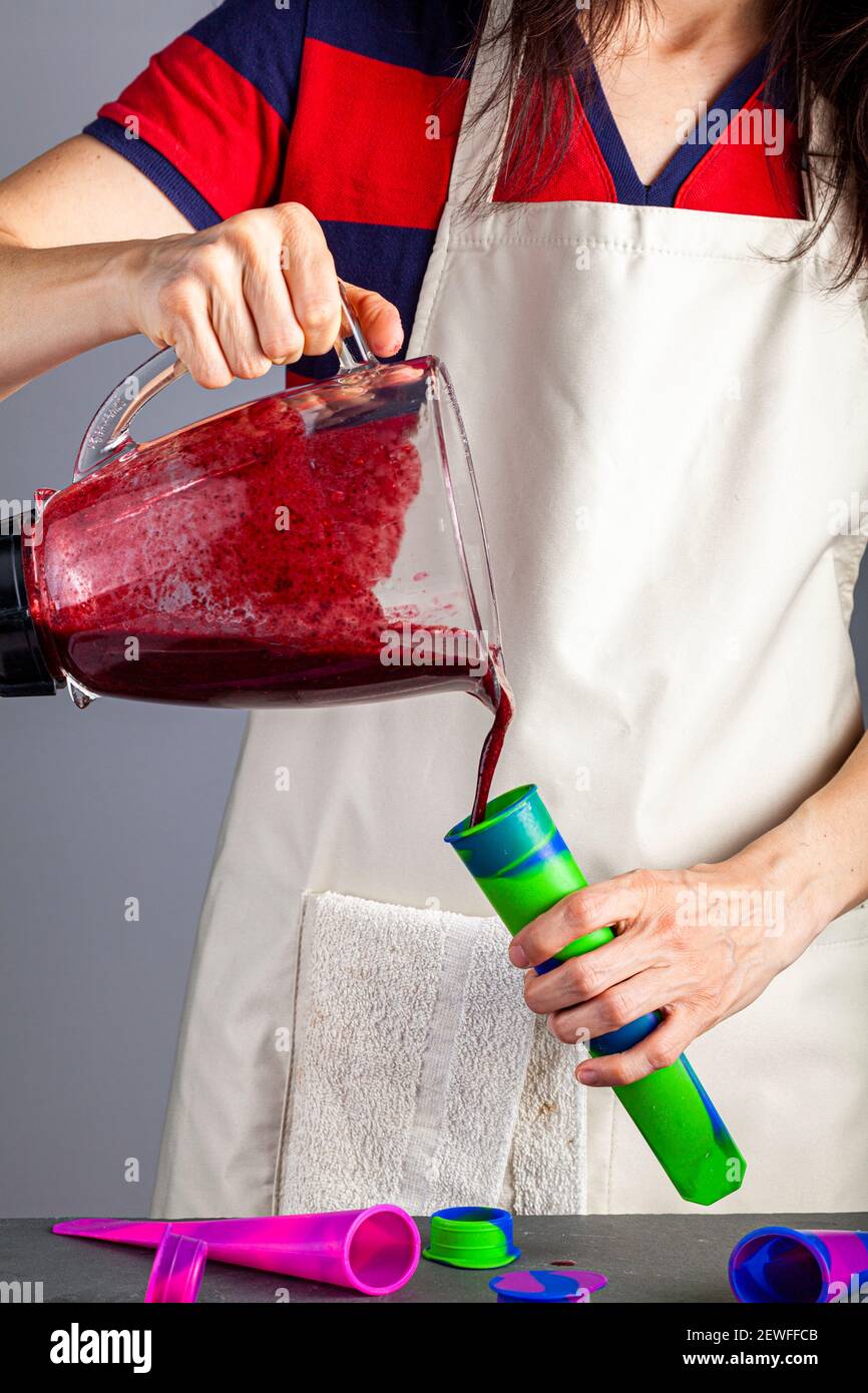 A caucasian mother wearing kitchen apron is pouring berry puree she ...