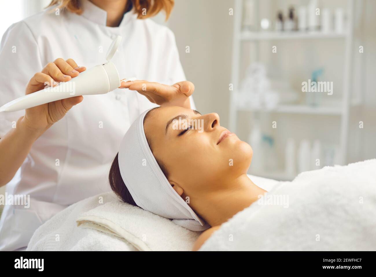 Cosmetologist Pouring Cream Before Facial Massage For Young Woman In