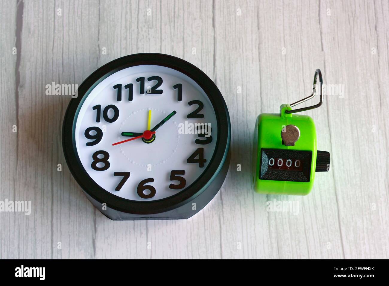 Green tally counter or hand counter with alarm clock on the wooden ...