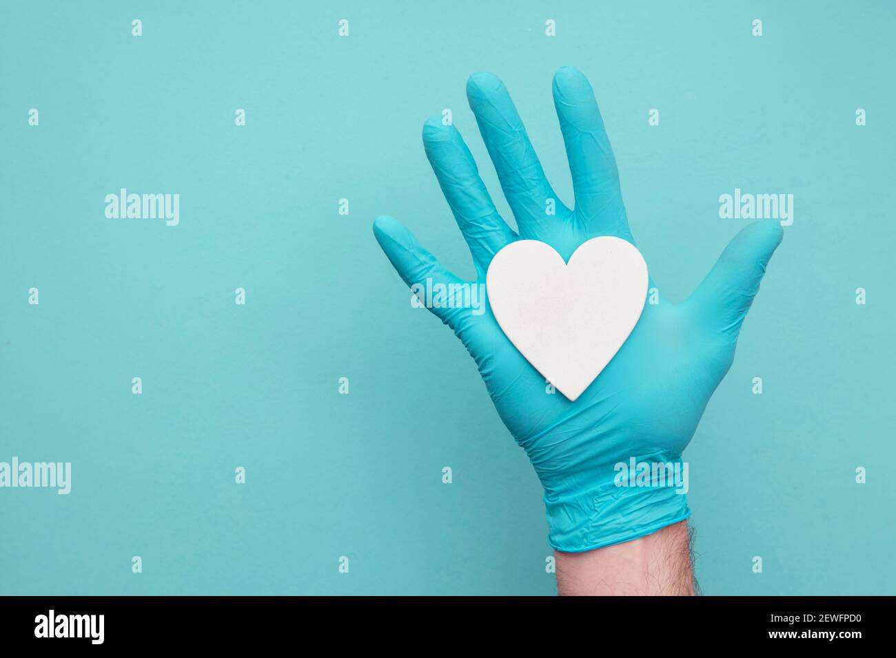 Doctors hands wearing blue surgical gloves holding a white heart shape ...