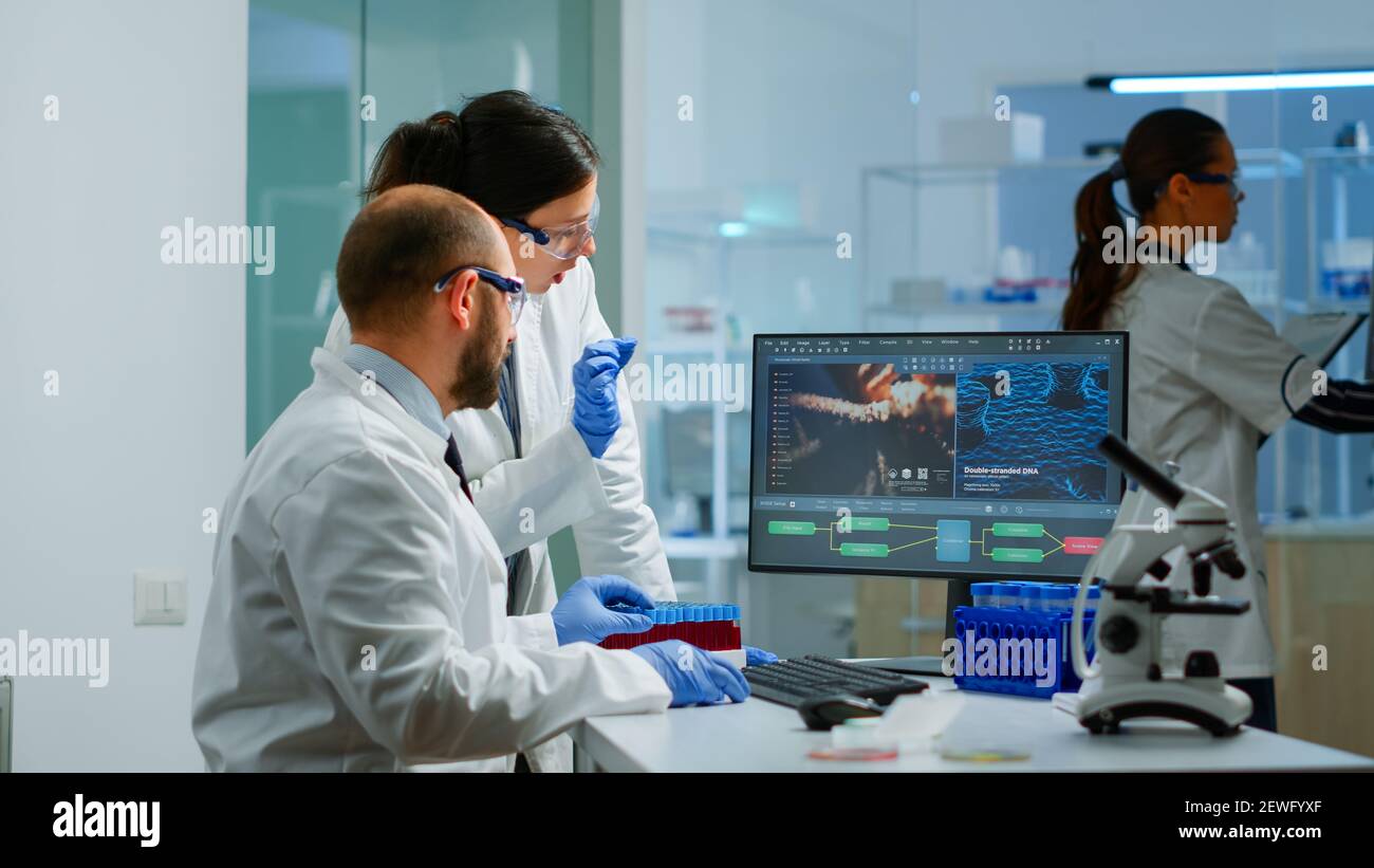 Team medical scientist conducting DNA experiments looking in computer ...