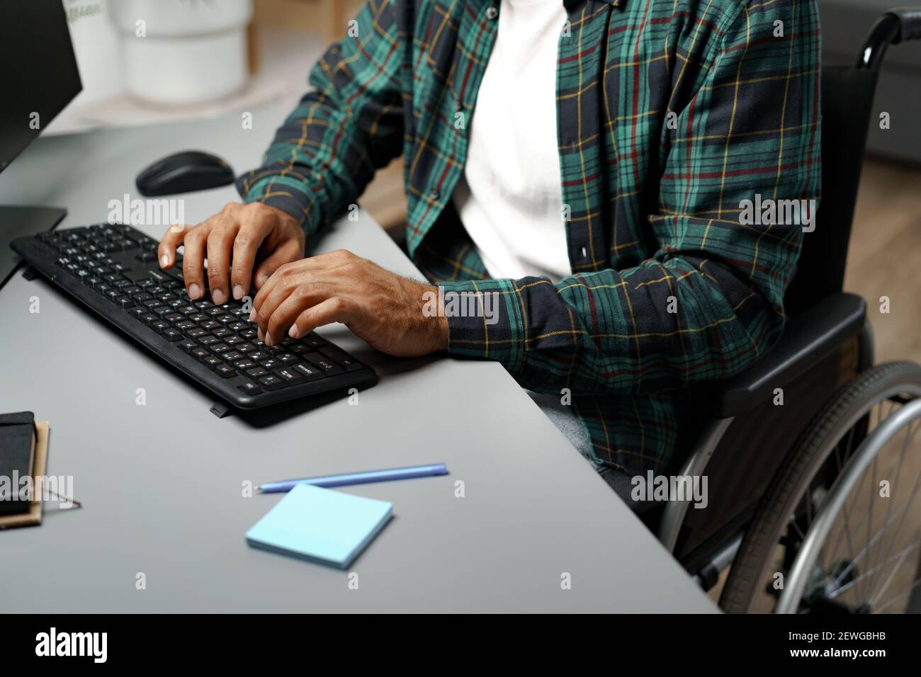 Disabled young african american man in wheelchair using computer while ...
